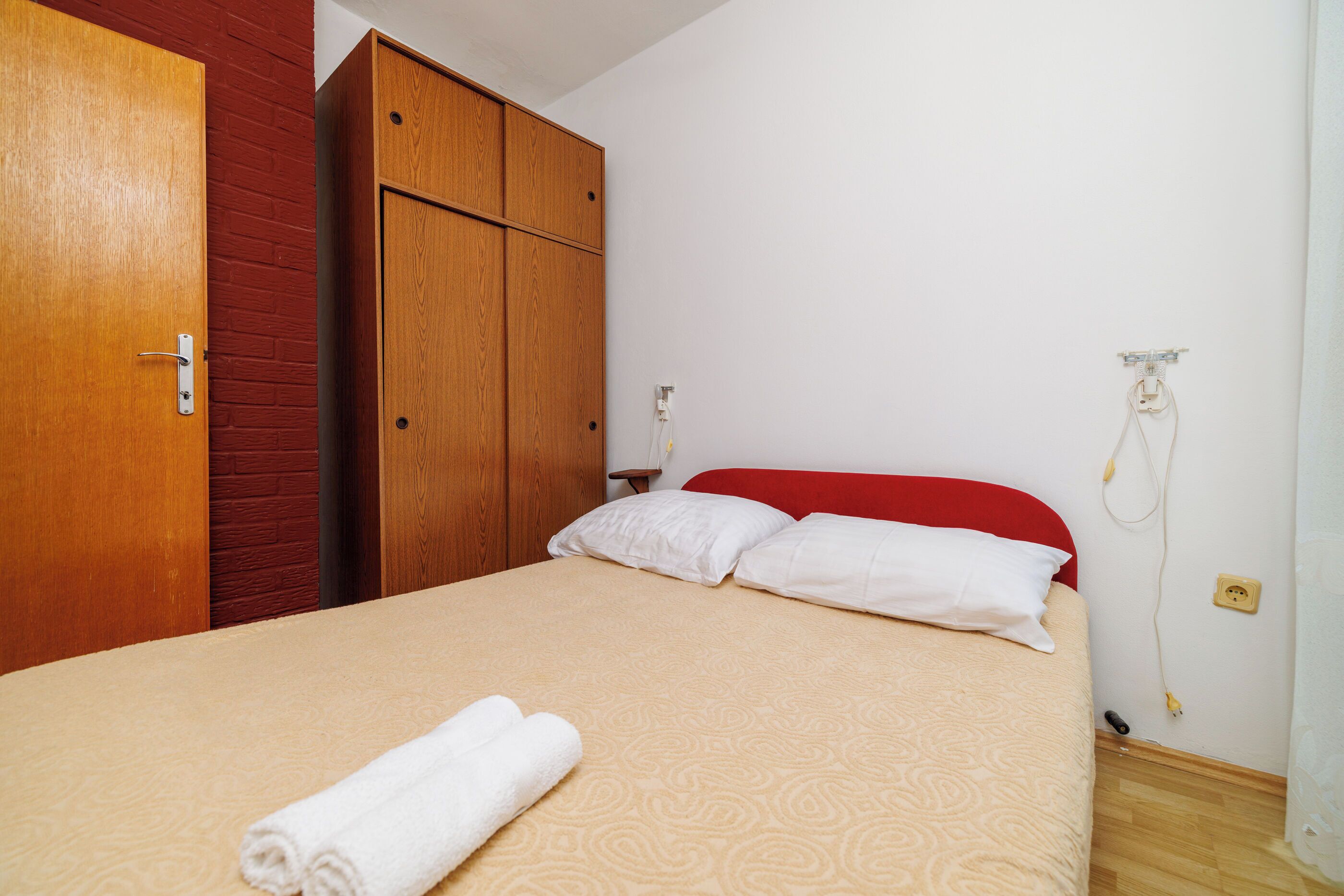 Quarto de hotel com cama, guarda-roupa de madeira e cabeceira vermelha.