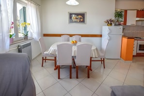 Uma área de refeições com uma mesa posta para quatro pessoas, geladeira e uma janela com cortinas.