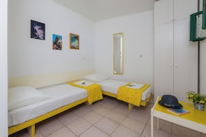 Quarto com duas camas de solteiro, uma pequena mesa com chapéu e livro, e um espelho na parede.