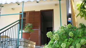 Um edifício com uma escadaria de pedra que leva a uma porta de madeira, um vaso com planta e folhagem verde.