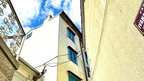 Uma rua estreita com um edifício que apresenta uma porta azul e uma escadaria que leva até ele.