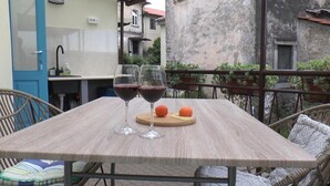 Uma mesa de madeira com duas taças de vinho e duas laranjas numa varanda com cadeiras de vime.