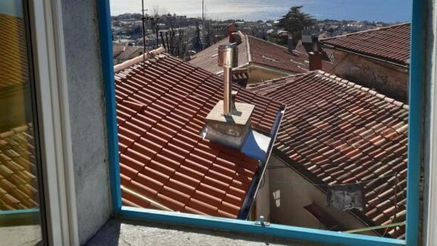 Vista da janela sobre uma área costeira com telhados de terracota e céu claro.