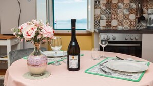 Mesa de jantar posta com uma garrafa de vinho, um vaso de flores e vista para a cozinha e exterior.