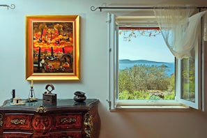 Quarto com uma grande janela que oferece vista para uma paisagem com árvores e colinas.