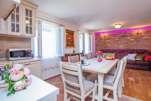 Uma área de refeições com uma mesa e cadeiras brancas, um buquê de flores e uma parede de tijolos com luz neon.