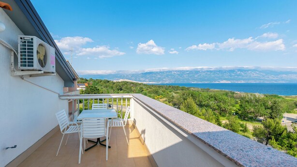 Varanda com mesa e cadeiras, vista para a paisagem costeira com árvores e o mar.