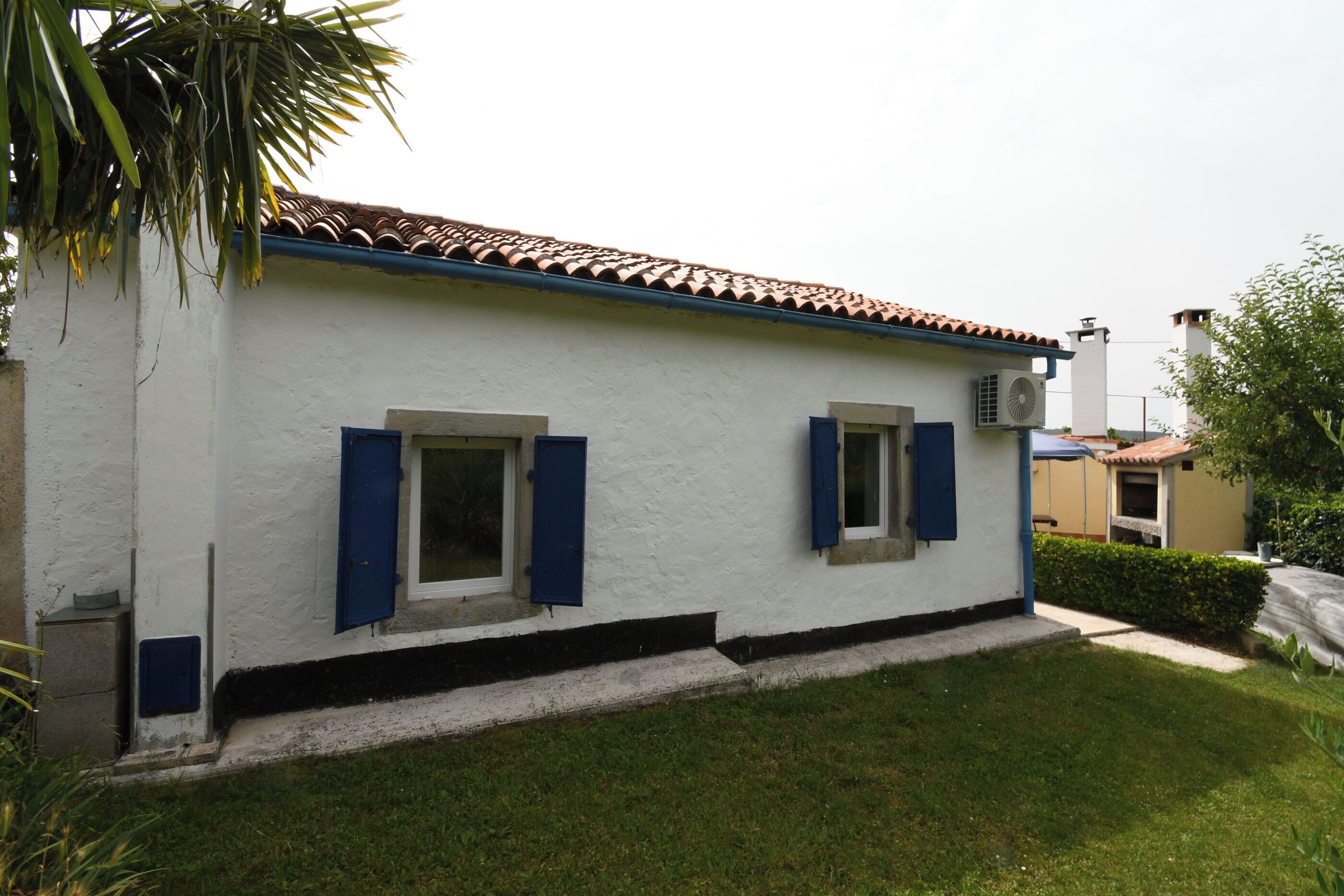 Um edifício branco com persianas azuis, telhado em telhas e um pequeno jardim frontal.