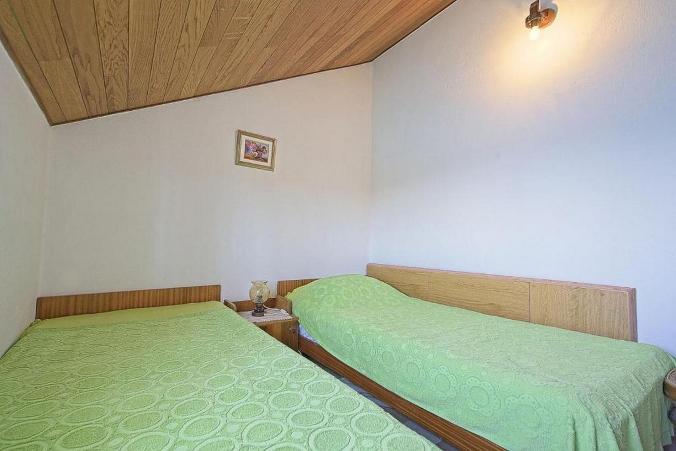Quarto com duas camas, cabeceiras de madeira, mesa de cabeceira pequena com abajur e um quadro pendurado na parede.