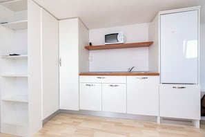 Uma cozinha compacta com armários brancos, um micro-ondas numa prateleira de madeira e uma geladeira.
