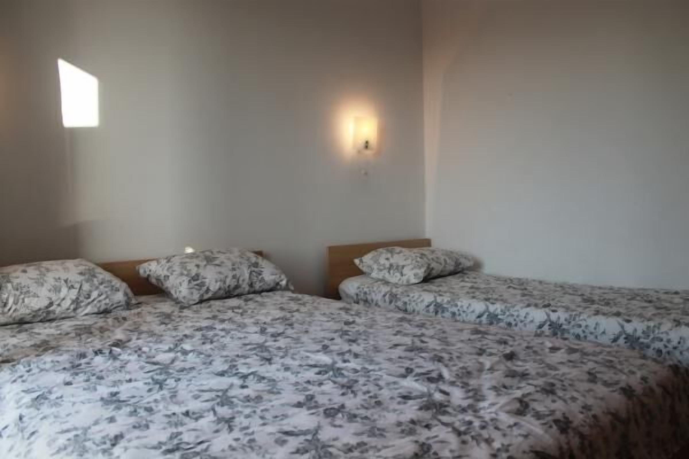 Quarto com duas camas, cada uma com roupa de cama estampada com motivos florais e cabeceiras de madeira.