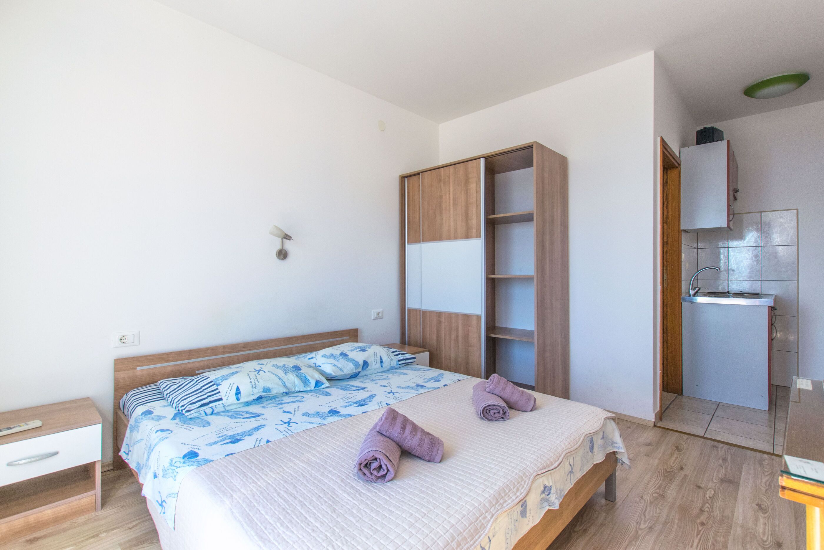 Quarto com cama, guarda-roupa, mesa de cabeceira e uma pequena cozinha.
