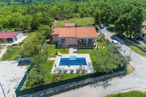 Uma casa com piscina, cercada por vegetação e um quintal murado.
