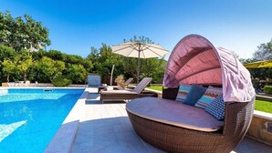 Uma área à beira da piscina com uma cadeira de vime, espreguiçadeiras e um espaço coberto para relaxar.