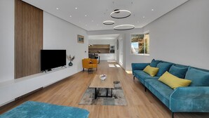 Uma sala de estar moderna com TV de tela plana, um sofá azul com almofadas amarelas, uma parede de destaque em madeira e iluminação embutida no teto.