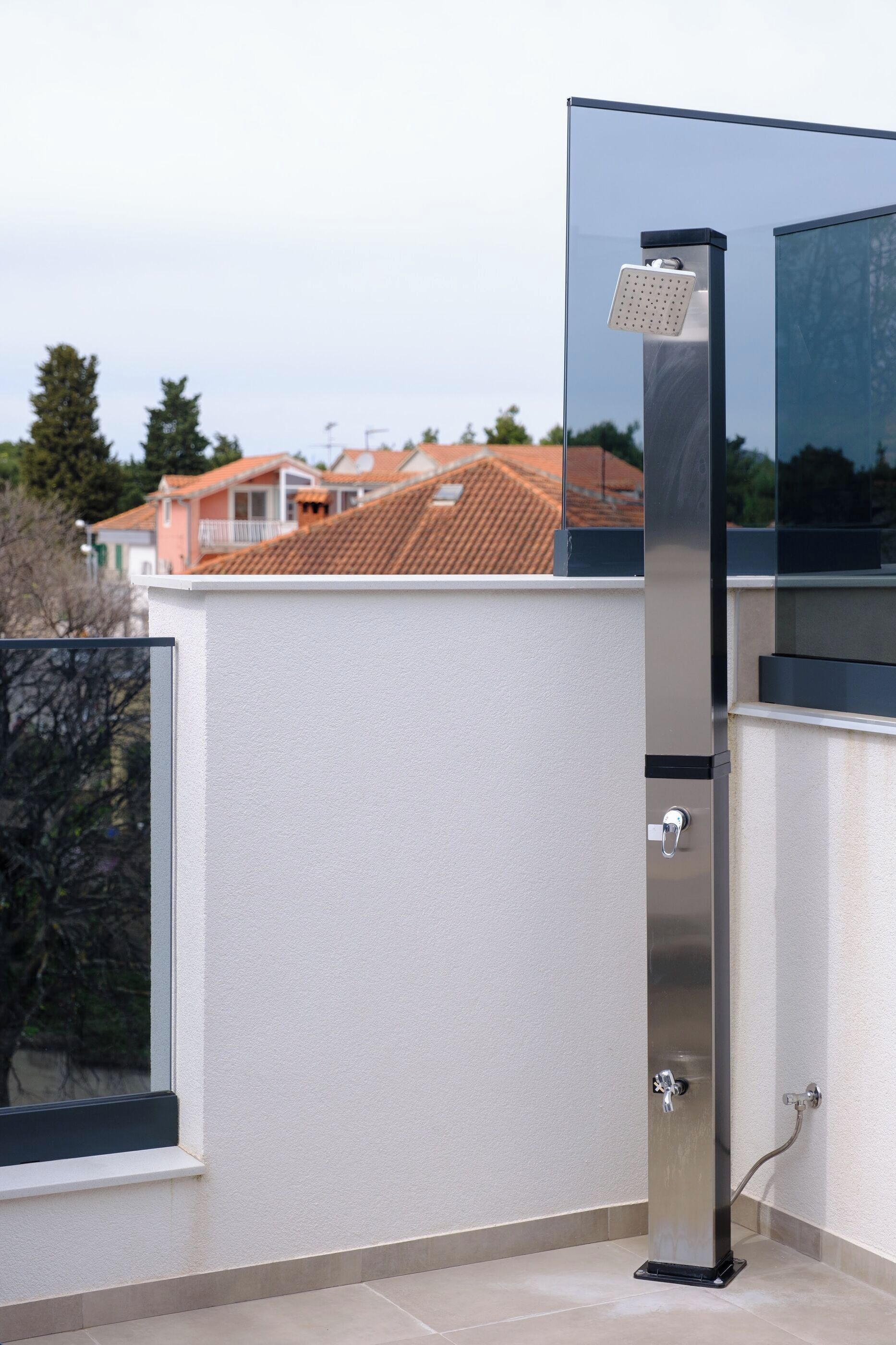 Um chuveiro exterior moderno com estrutura de vidro, uma maçaneta de metal e uma mangueira.