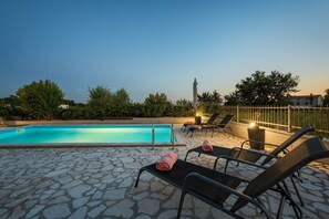 Piscina com espreguiçadeiras e deck de ladrilho.