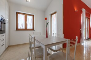 Uma sala de jantar com uma mesa e cadeiras brancas, um vaso com uma flor vermelha e uma parede vermelha.