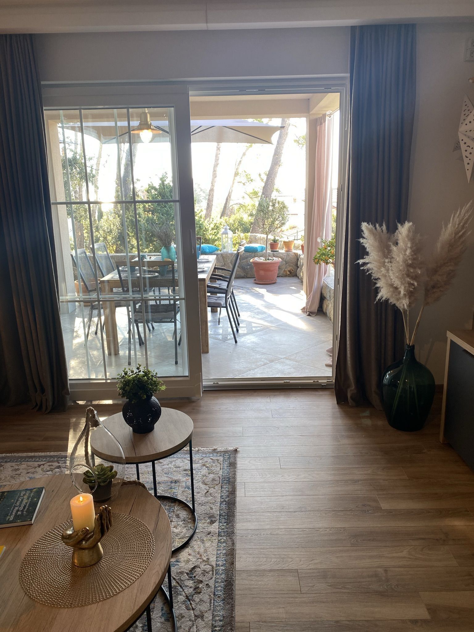 Quarto com vista para um pátio, uma mesa de madeira redonda com uma vela, um vaso com plumas de capim-do-campo e uma planta em vaso.