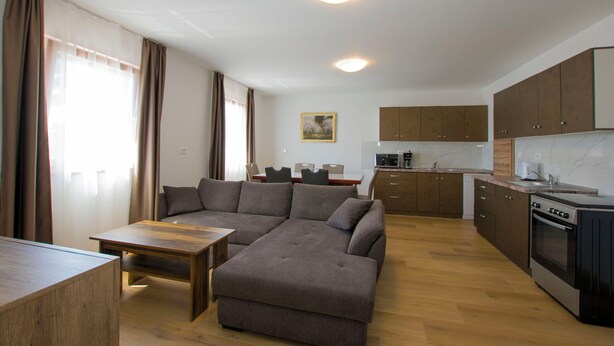 Uma sala de estar moderna com um sofá seccional, uma mesa de centro de madeira e uma área de cozinha com armários de madeira e forno embutido.