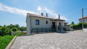Uma casa de dois andares com telhado de telhas, uma pequena varanda frontal e um caminho de entrada pavimentado.