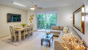 Uma sala de estar moderna com área de jantar, sofá, mesa de centro e uma grande janela com vista para o verde.