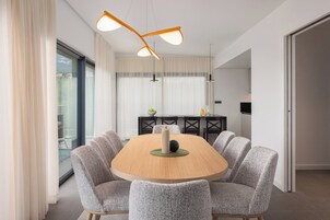Uma sala de jantar moderna com uma mesa redonda, seis cadeiras estofadas e iluminação pendente.