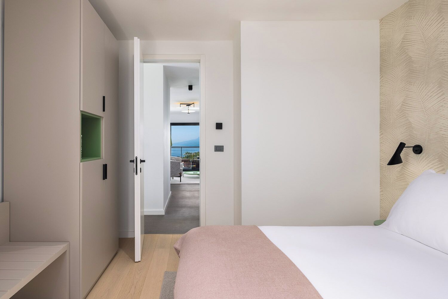 Quarto com cama, mesa de cabeceira, escrivaninha e vista para uma varanda.