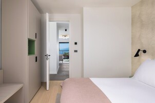 Quarto com cama, mesa de cabeceira, escrivaninha e vista para uma varanda.