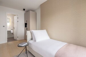 Quarto de hotel moderno com cama, mesa de cabeceira, guarda-roupa e banheiro visível através de uma porta aberta.