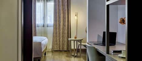 Quarto de hotel com uma cama, uma escrivaninha, uma cadeira e um espelho grande.