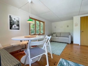 Sala de estar com mesa redonda, sofá e janela com vista para árvores.