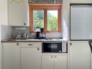 Cozinha compacta com micro-ondas embutido, cafeteira e janela com vista para o verde.