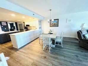 Cozinha moderna com armários brancos, uma ilha central e um espaço de jantar com mesa e cadeiras.