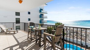 Uma varanda com piscina, cadeiras de madeira, uma mesa e vista para a praia.