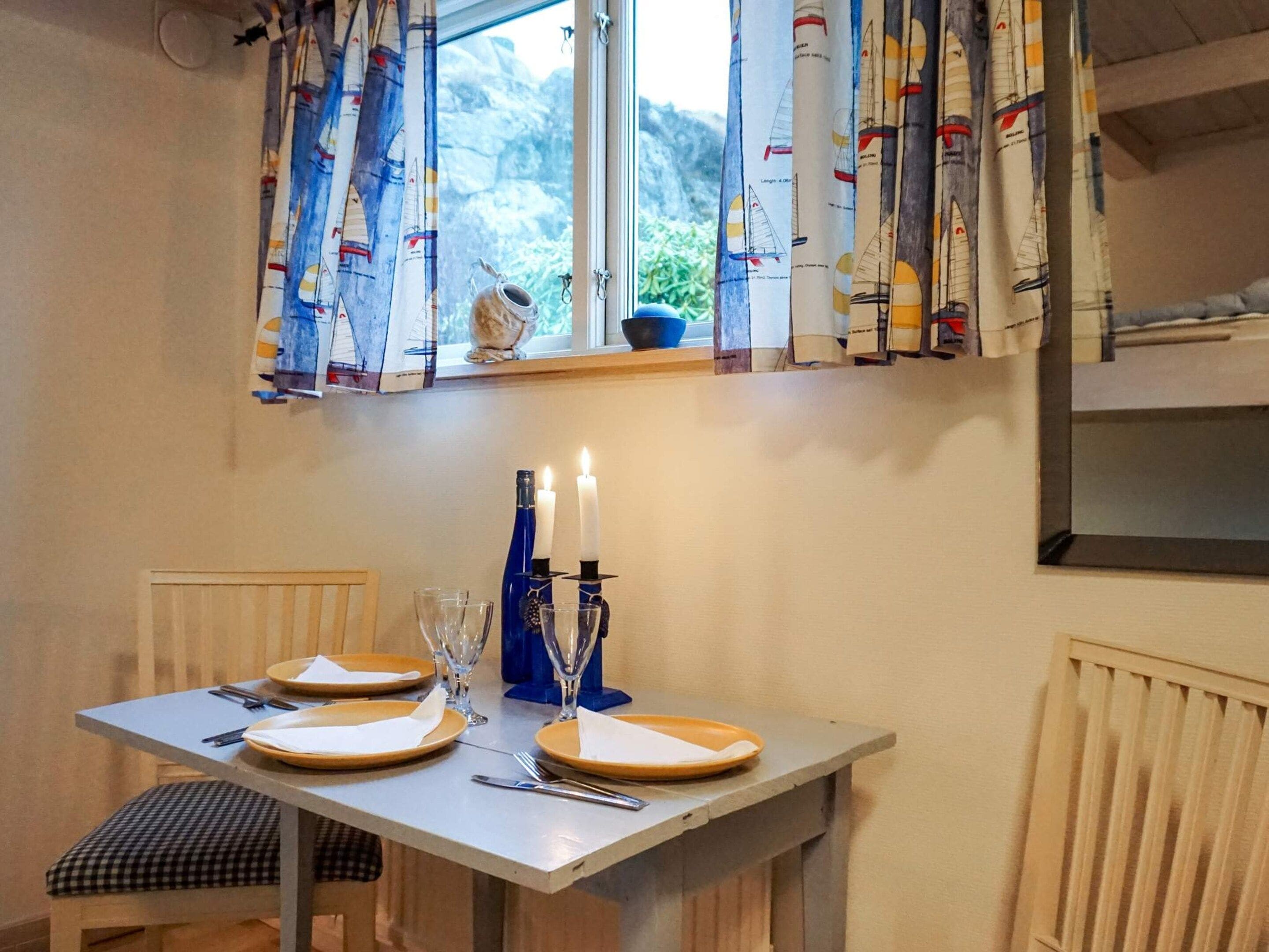 Uma sala de jantar com mesa posta para dois, janela com cortinas e vista para o verde lá fora.