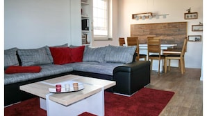 Uma sala de estar moderna com um sofá cinza, almofadas vermelhas, uma mesa de centro de madeira e um tapete vermelho.