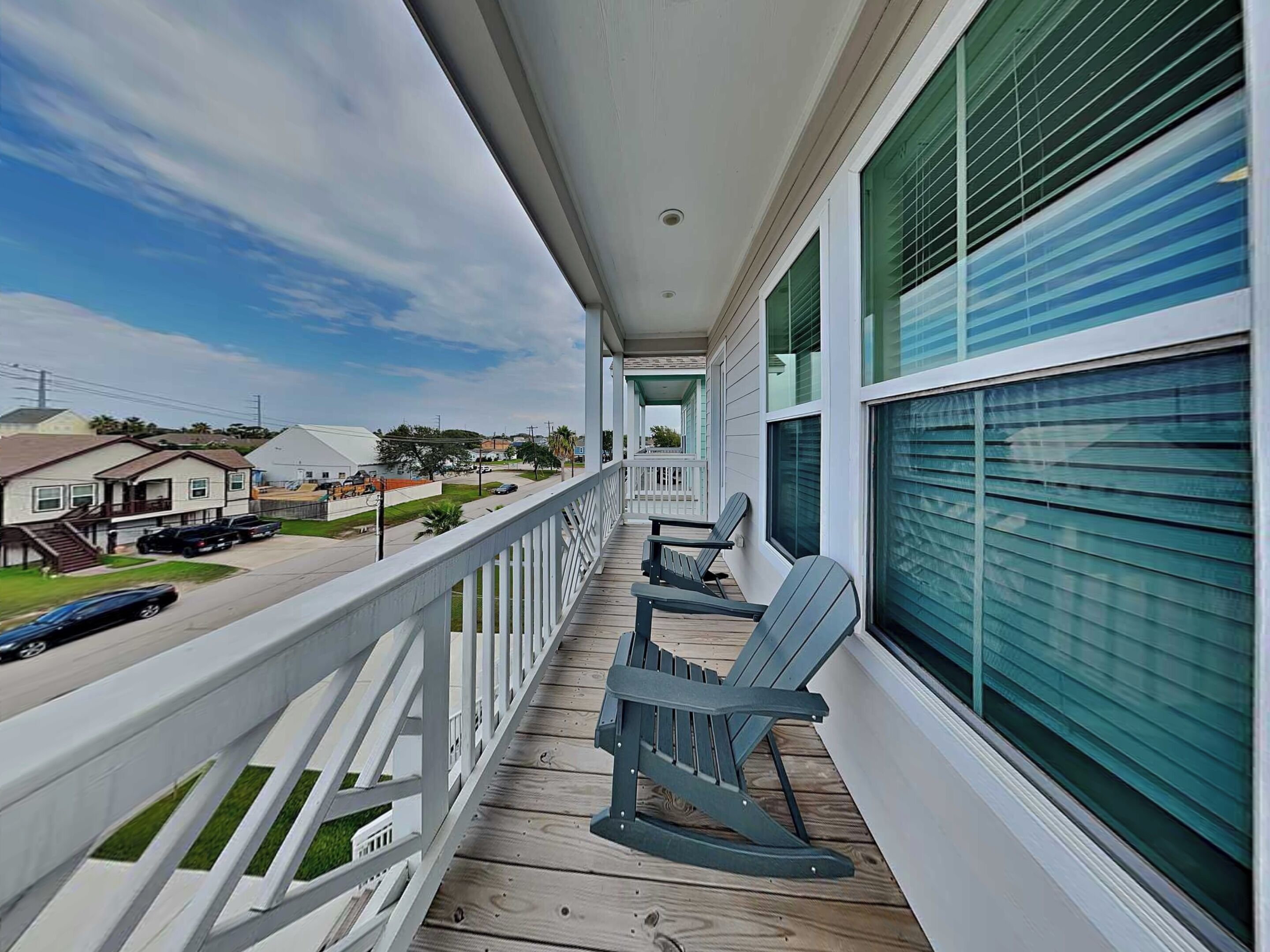 Um deck de madeira com cadeiras de balanço, um alpendre coberto e vista para uma rua residencial.