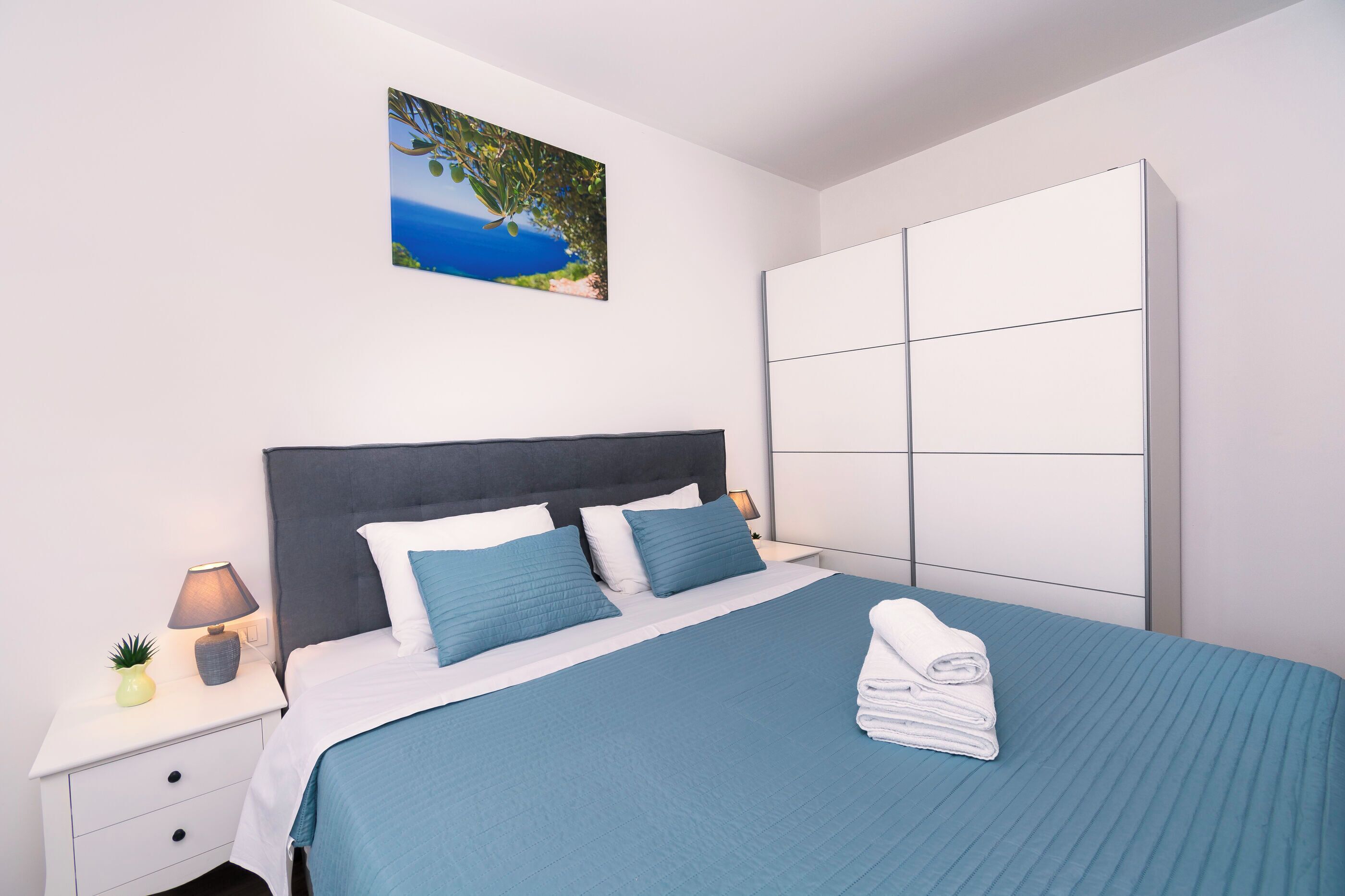 Um quarto moderno com uma cama, mesas de cabeceira, um quadro e um guarda-roupa.