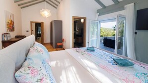 Quarto com cama grande, roupa de cama floral, ventilador de teto e vista para o exterior.