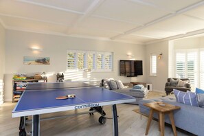 Uma sala de estar com mesa de pingue-pongue, sofá, mesa de centro e televisão.