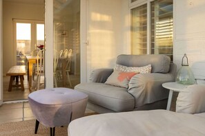 Uma sala de estar moderna com um sofá cinzento, um banquinho redondo e uma mesa pequena com cúpula de vidro.