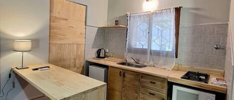 Cozinha compacta com bancada de madeira, micro-ondas embutido, fogão e pia.