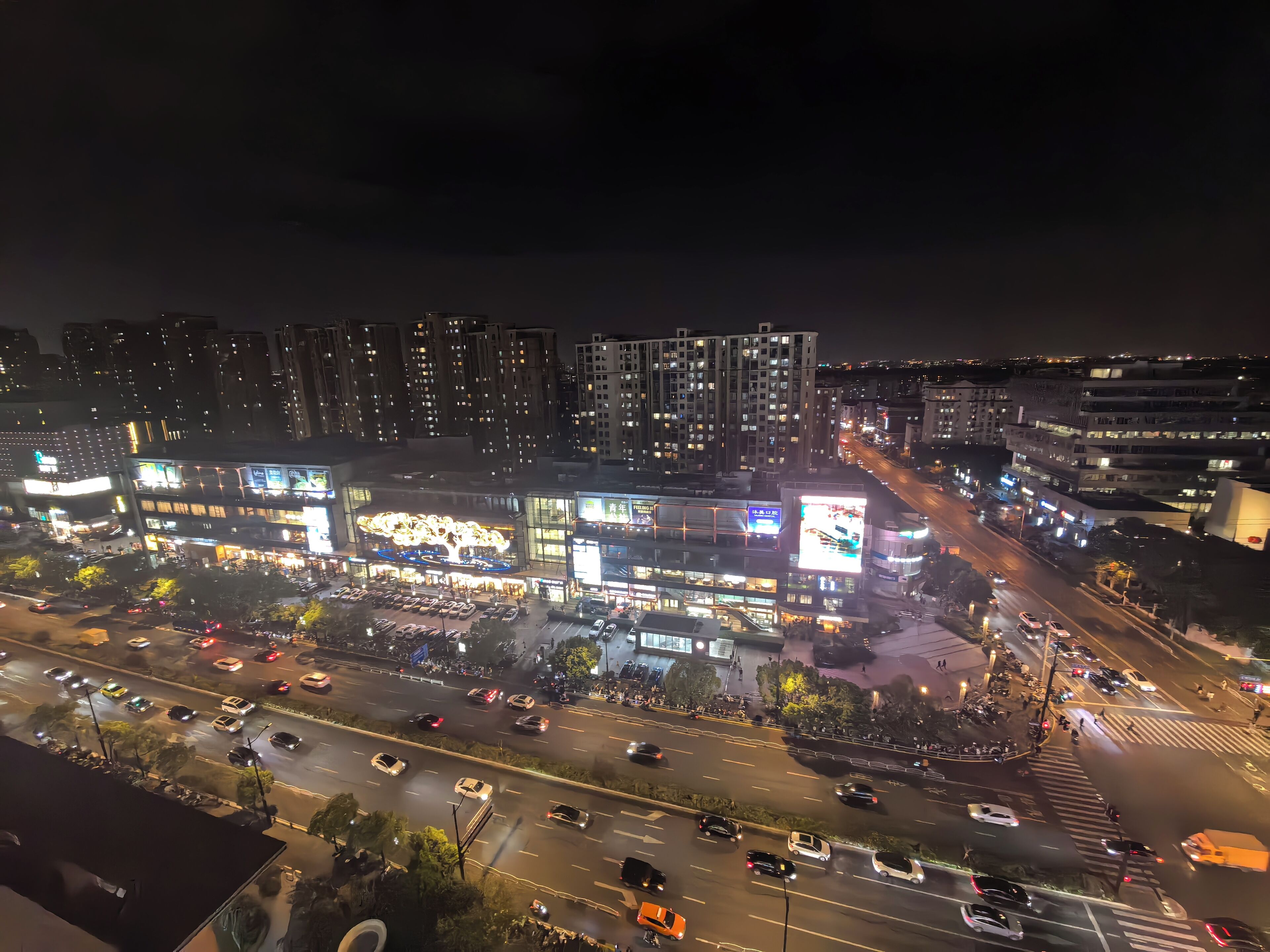 Paisagem urbana noturna com edifícios altos, ruas movimentadas e painéis luminosos iluminados.