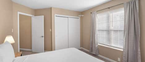 Quarto de hotel com cama, ventoinha no teto, janela com persianas e porta.