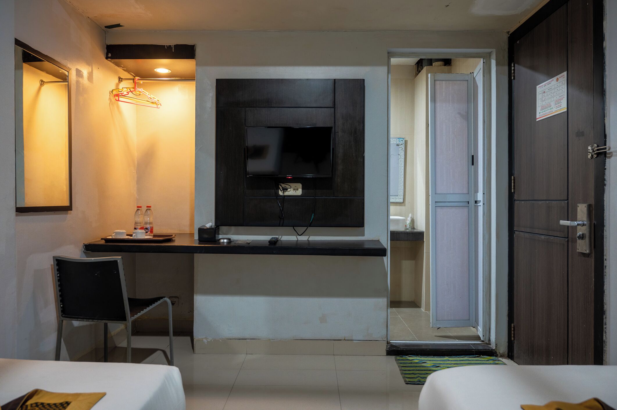 Quarto de hotel com cama, escrivaninha com cadeira, televisão na parede e armário.