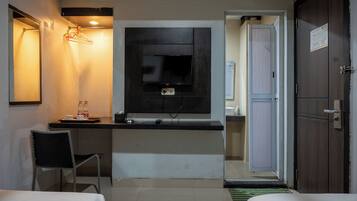 Quarto de hotel com cama, escrivaninha com cadeira, televisão na parede e armário.
