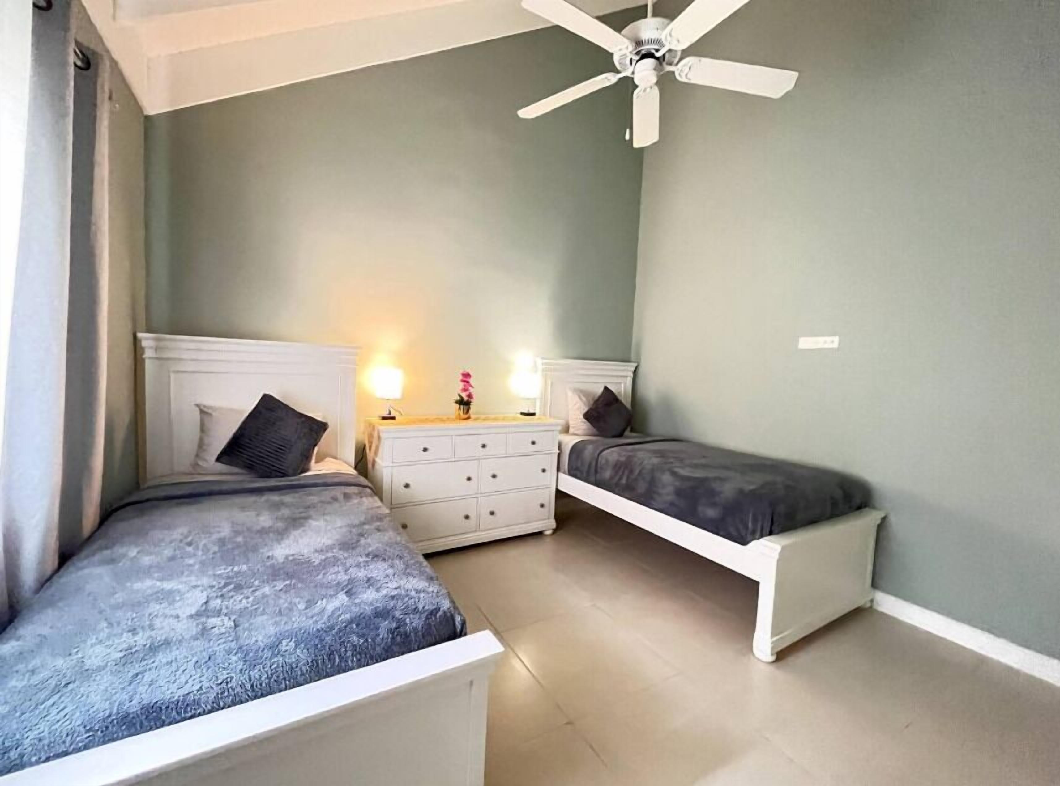 Quarto com duas camas, um ventilador de teto e luminárias de cabeceira.