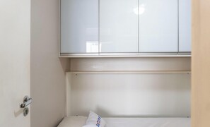 Quarto pequeno com uma cama de solteiro, um guarda-roupa branco sobre a cama e uma porta com puxador.