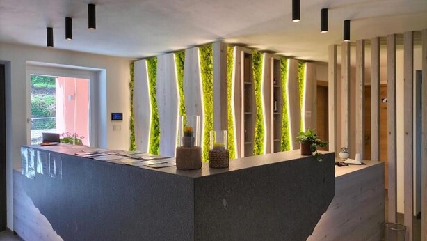 Uma área de recepção com design moderno, destacando um balcão curvo, ripas verticais de madeira e plantas verdes.